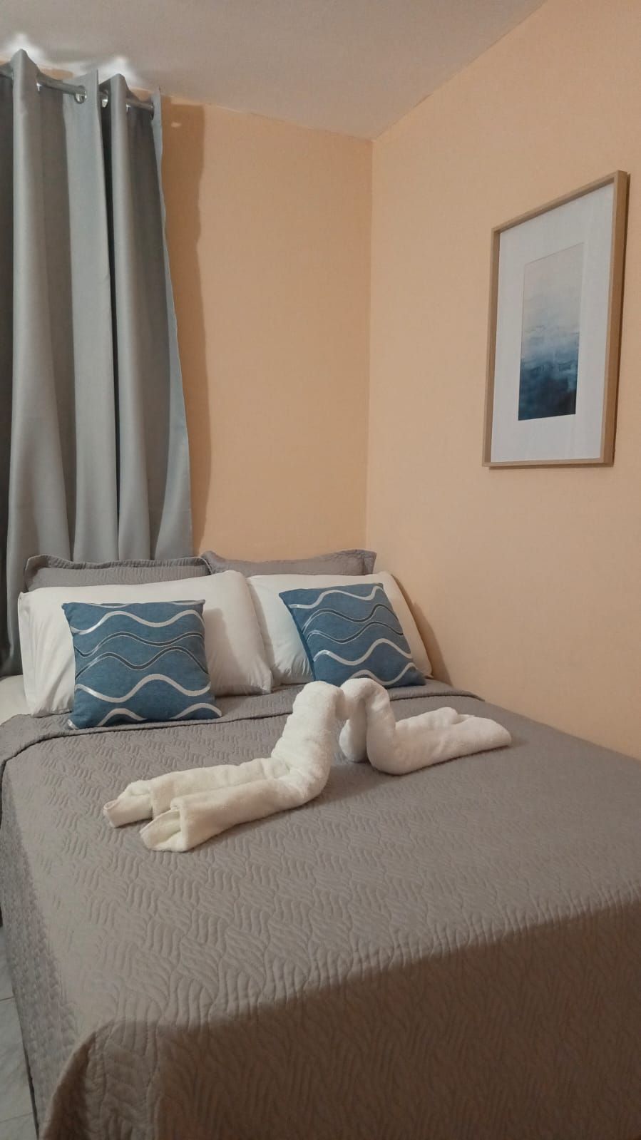 Cama bem arrumada com colcha cinza e duas almofadas com padrão de ondas azuis.
