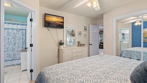 Quarto com cama, ventilador de teto, cômoda, espelho e janela.