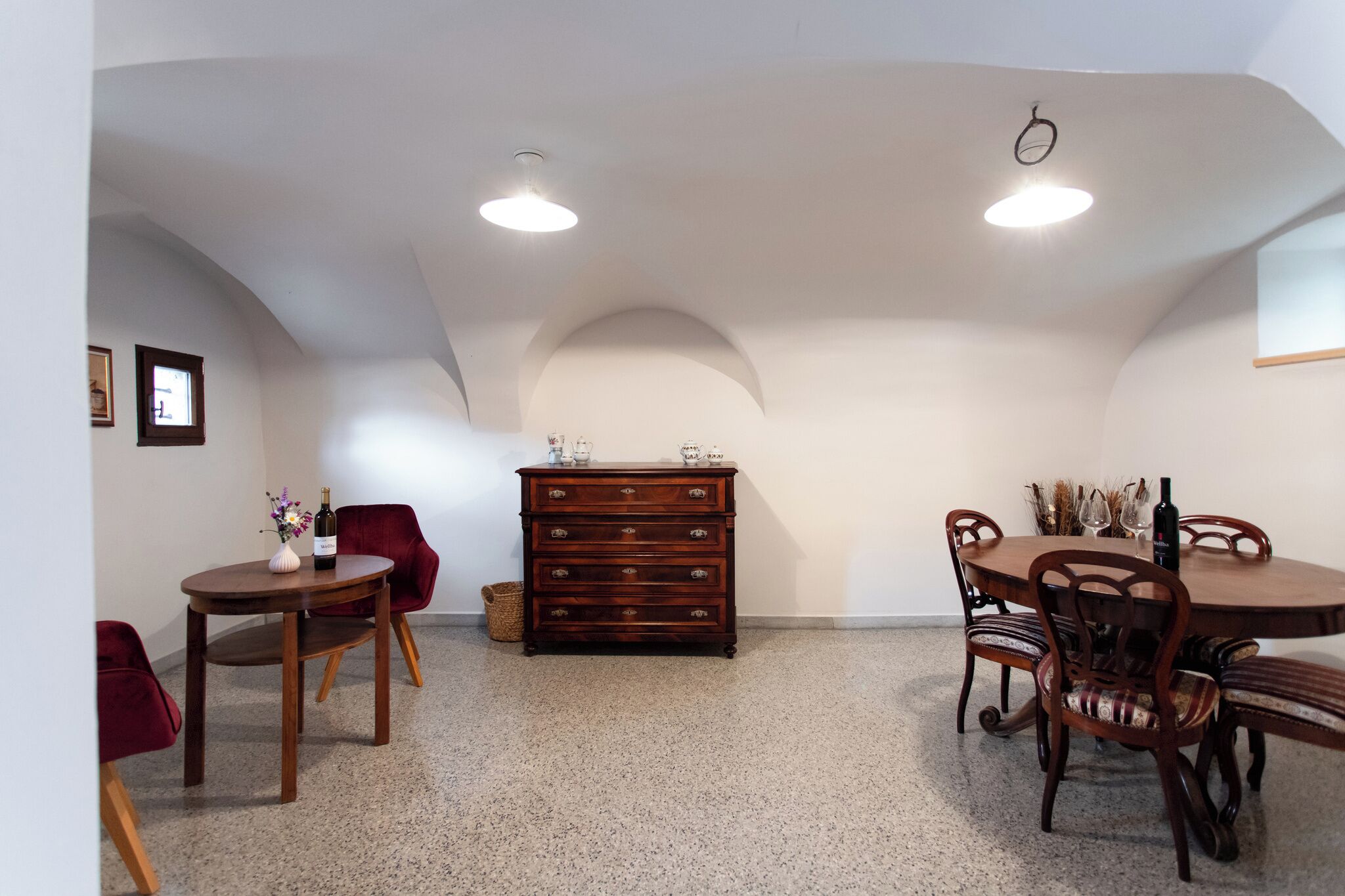 Uma sala de jantar com uma mesa redonda, cadeiras de madeira, um aparador de madeira e duas luminárias pendentes.