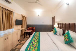 Quarto de hotel com cama, escrivaninha, cadeira, televisão e ventoinha no teto.