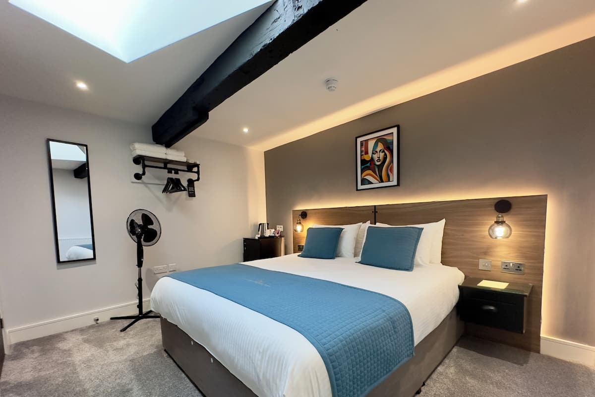 Quarto moderno com uma cama grande, um ventilador de teto, uma mesinha de cabeceira com abajur e uma obra de arte na parede.