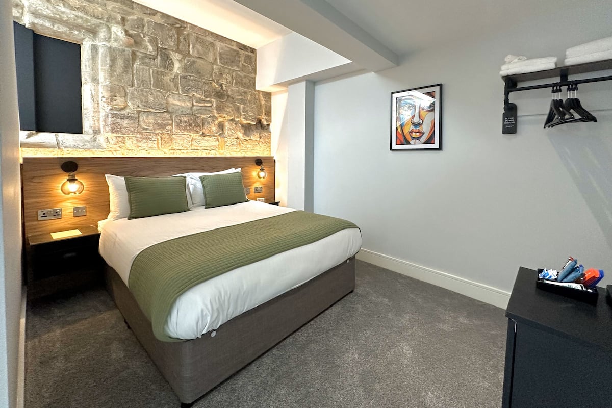 Quarto com parede de destaque em pedra, cama com roupa de cama verde, obra de arte pendurada e sapateira.