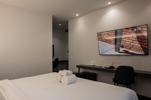 Quarto de hotel com cama, escrivaninha, televisão de tela plana na parede e uma pequena mesa com um copo d'água.