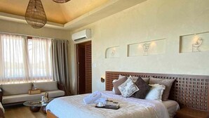 Quarto de hotel moderno com uma cama grande, um sofá, uma mesinha e uma janela com cortinas.