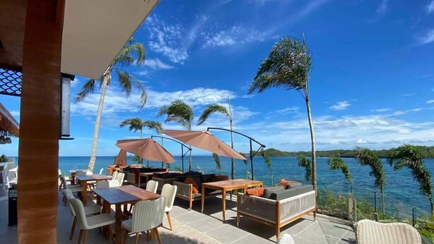 Uma área de estar ao ar livre com mesas, cadeiras, guarda-sóis e vista para o mar.