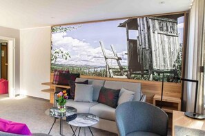 Uma sala de estar moderna com um sofá, uma poltrona, uma mesa de centro e um quadro de uma estrutura de madeira.