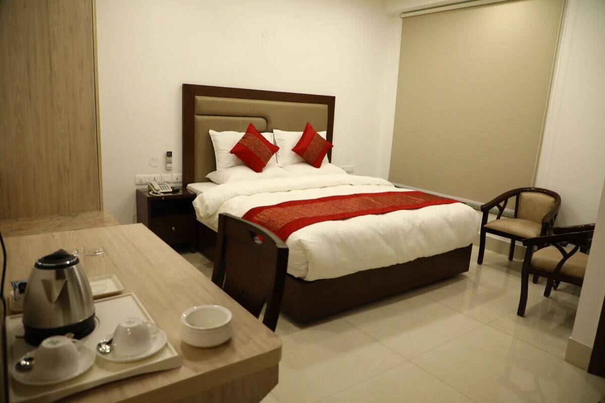Quarto de hotel com cama, mesa de cabeceira, cafeteira, chávenas e um tabuleiro.