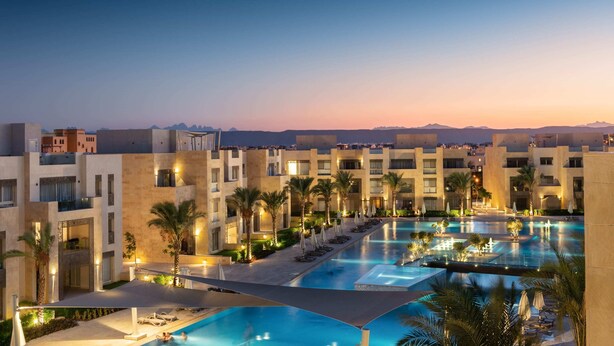 Resort com várias piscinas, palmeiras e edifícios modernos.