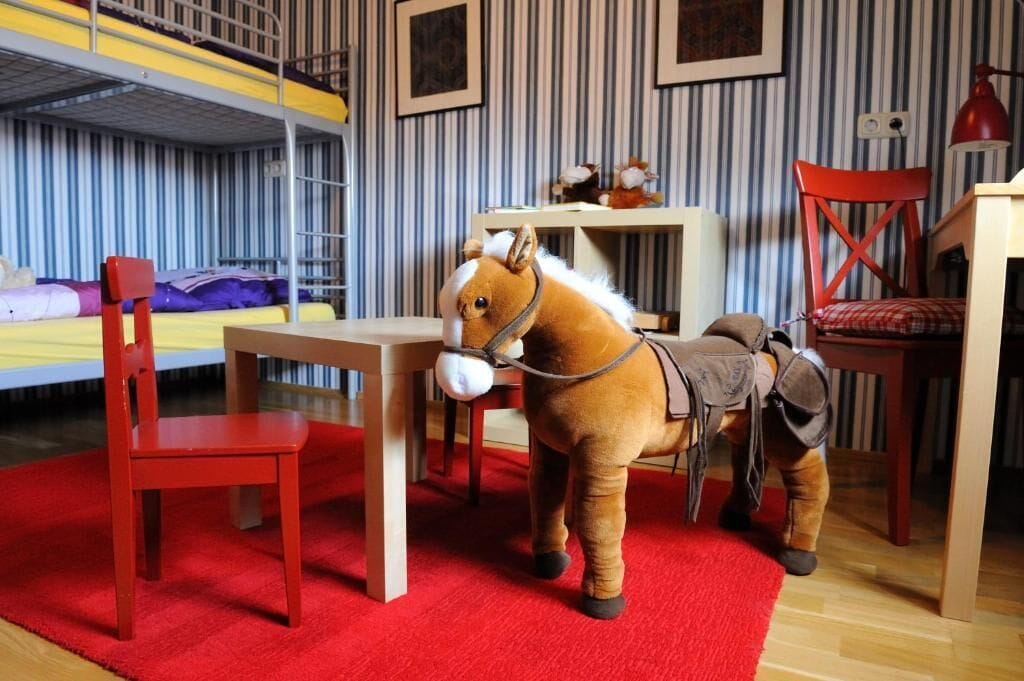 Uma cama beliche, uma mesa de madeira, uma cadeira vermelha, um brinquedo de cavalo de pelúcia e papel de parede listrado.