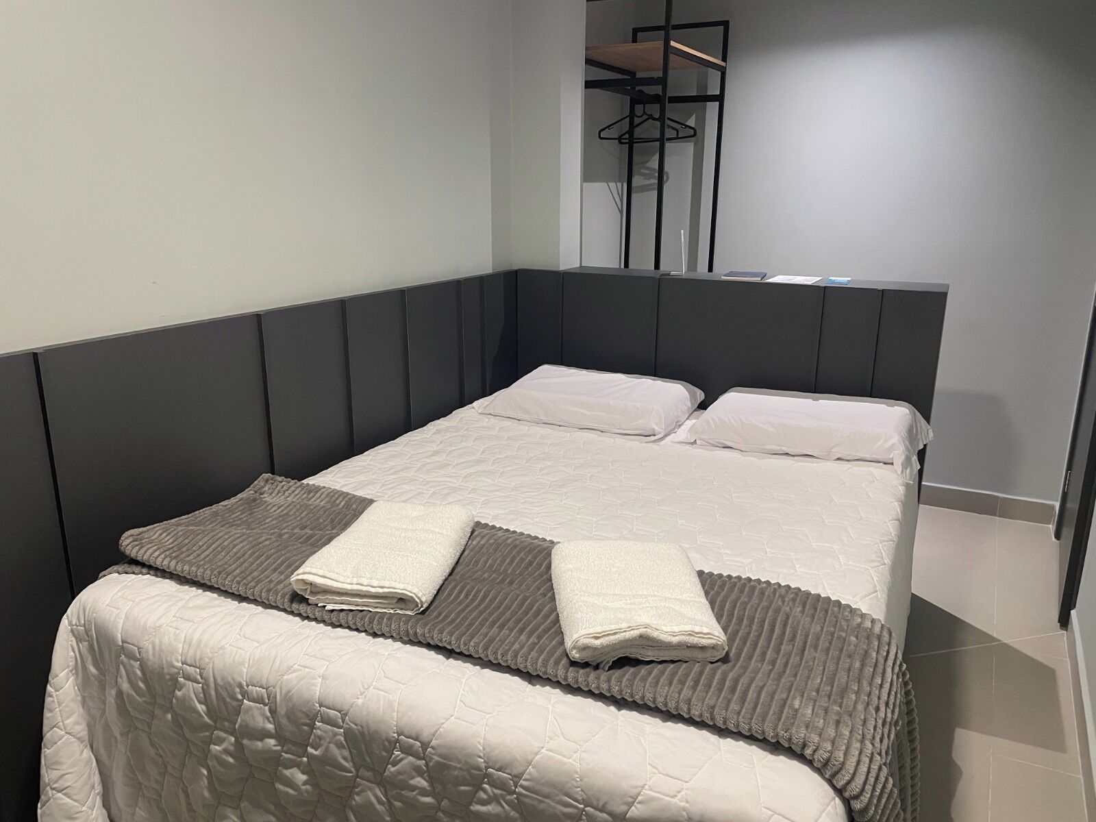 Uma cama de solteiro com cabeceira, mesa de cabeceira e cabideiro.