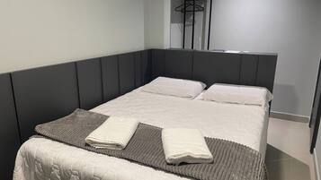 Uma cama de solteiro com cabeceira, mesa de cabeceira e cabideiro.