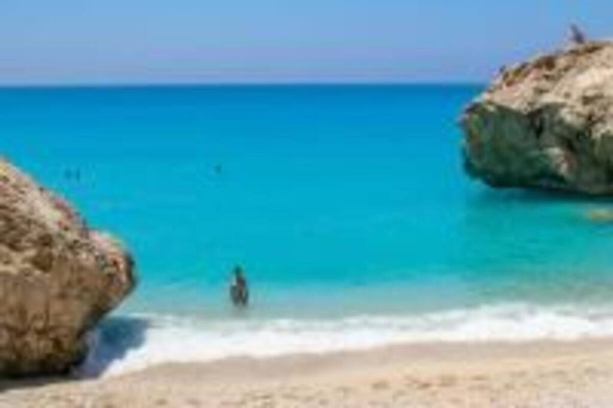 Uma praia com águas turquesa cristalinas, um afloramento rochoso e uma pessoa nadando.