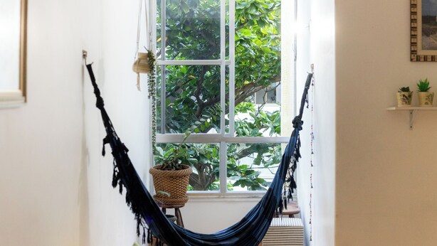 Quarto com rede, janela com vista para vegetação e prateleira com plantas em vasos.