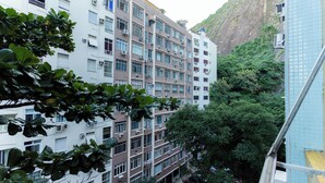 Um edifício residencial com várias andares e varandas, cercado por vegetação exuberante e com uma montanha ao fundo.