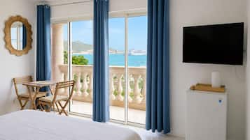 Quarto de hotel com cama, escrivaninha com cadeiras, televisão e varanda com cortinas.