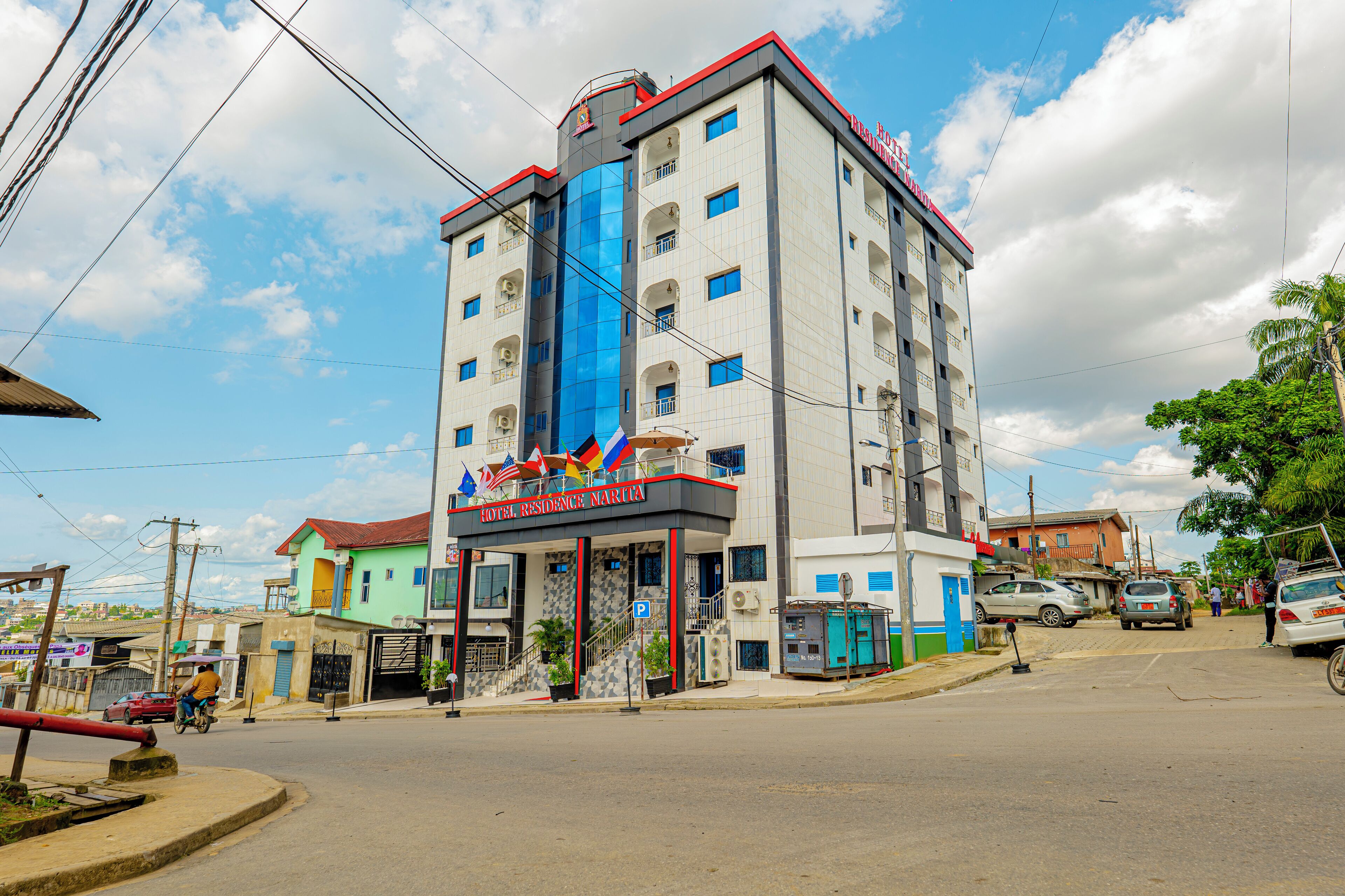 Hotel com vários andares, entrada destacada, fachada de vidro azul vertical e telhado vermelho e branco.