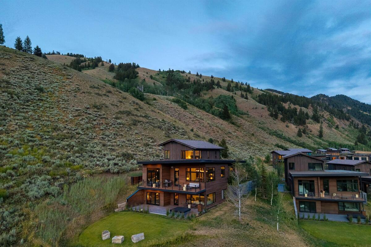 Uma casa moderna de dois andares com uma varanda ampla, emoldurada por uma paisagem montanhosa.
