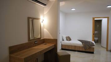 Quarto moderno com toucador de madeira, cama com manta e banheiro visível através de uma porta aberta.