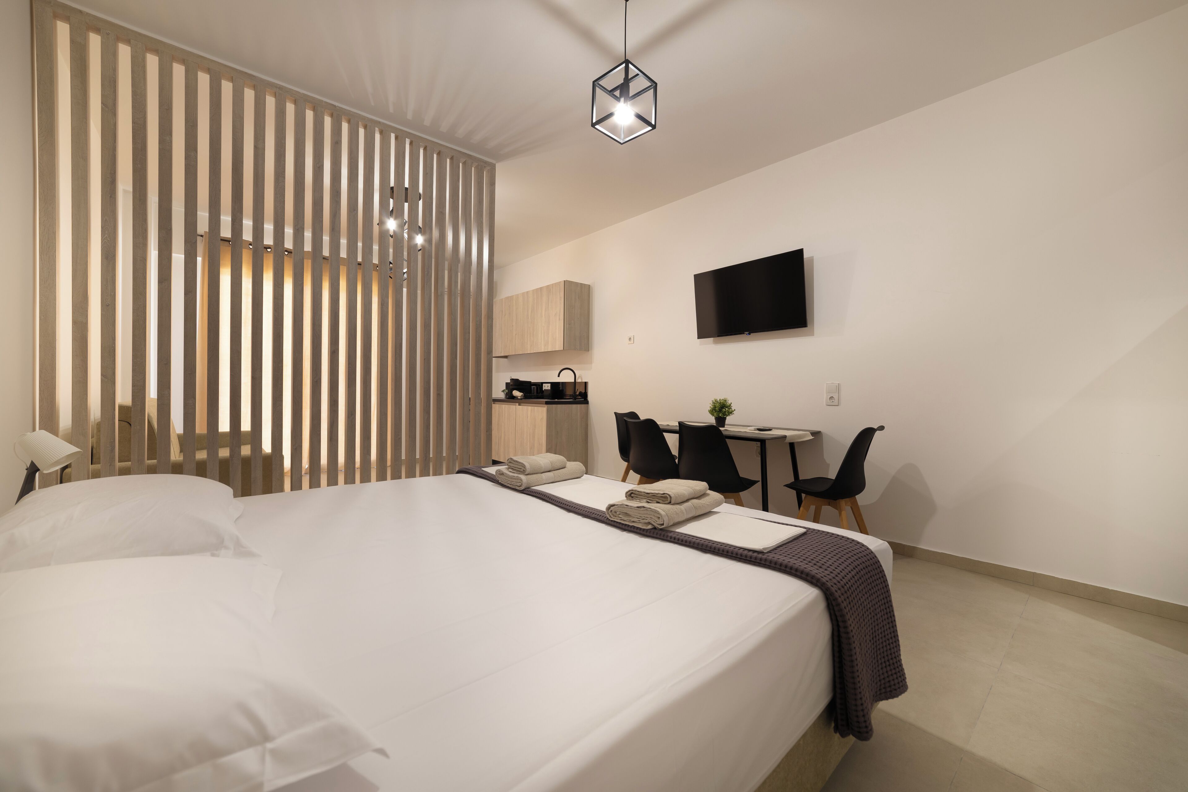 Quarto de hotel moderno com uma cama grande, uma escrivaninha, uma cadeira, uma televisão e uma cozinha.