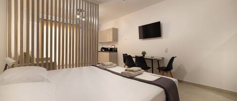 Quarto de hotel moderno com uma cama grande, uma escrivaninha, uma cadeira, uma televisão e uma cozinha.