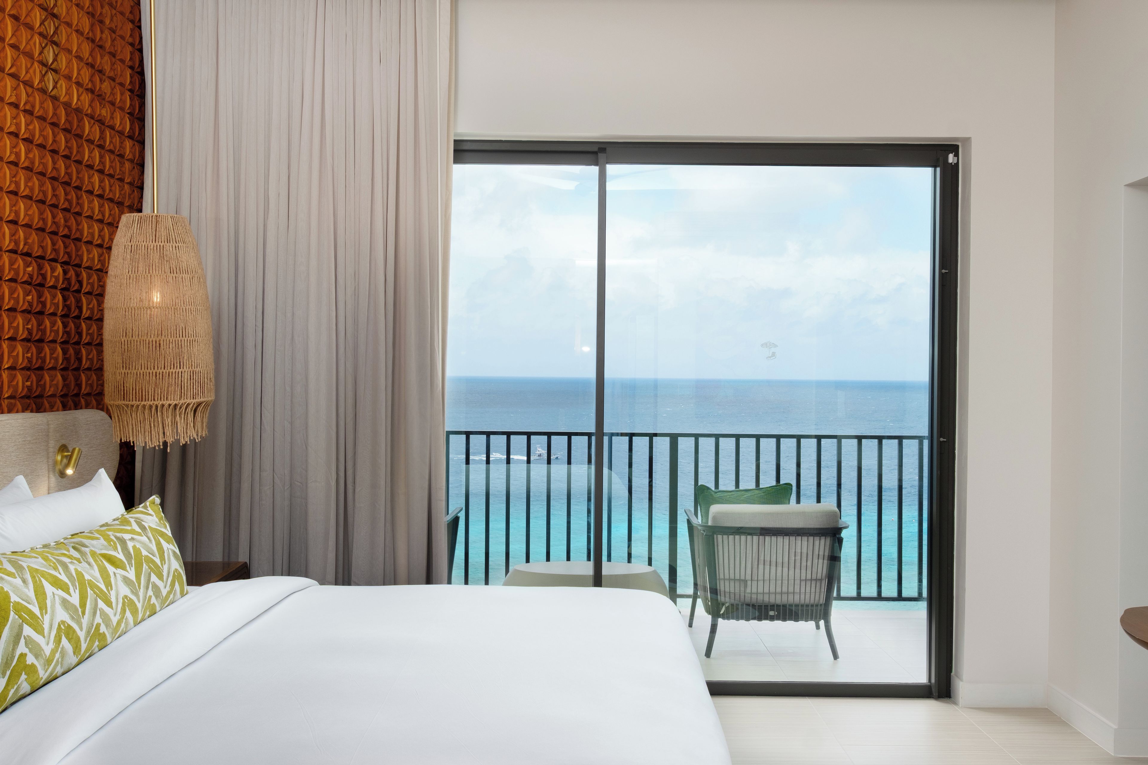 Quarto de hotel com cama, cadeira, varanda e vista para o mar, além de uma janela grande.
