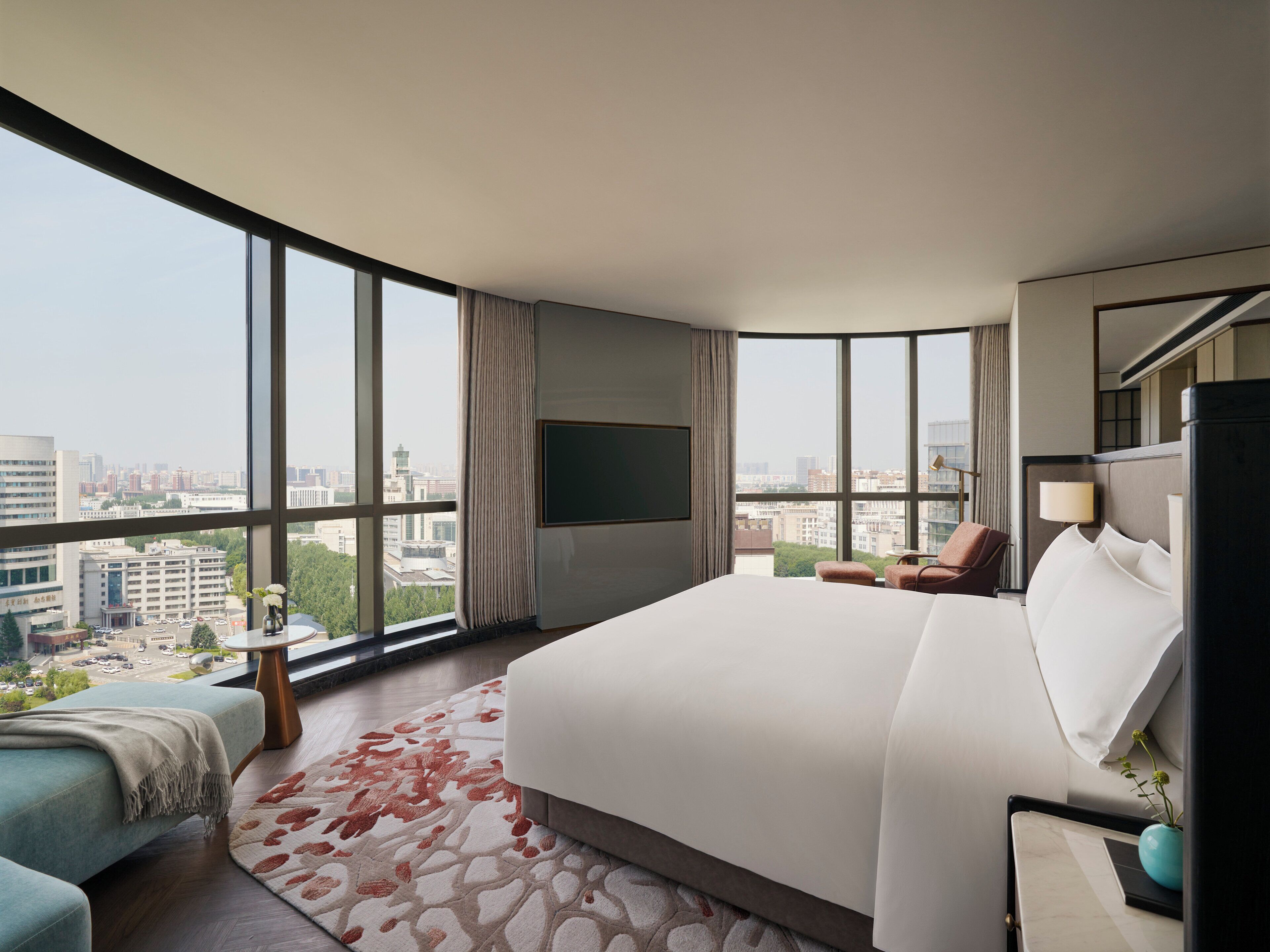 Quarto de hotel com uma cama grande, televisão, área de estar e vista da cidade.