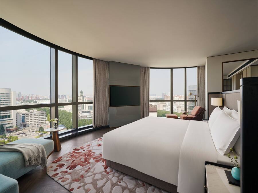 Quarto de hotel com uma cama grande, televisão, área de estar e vista da cidade.