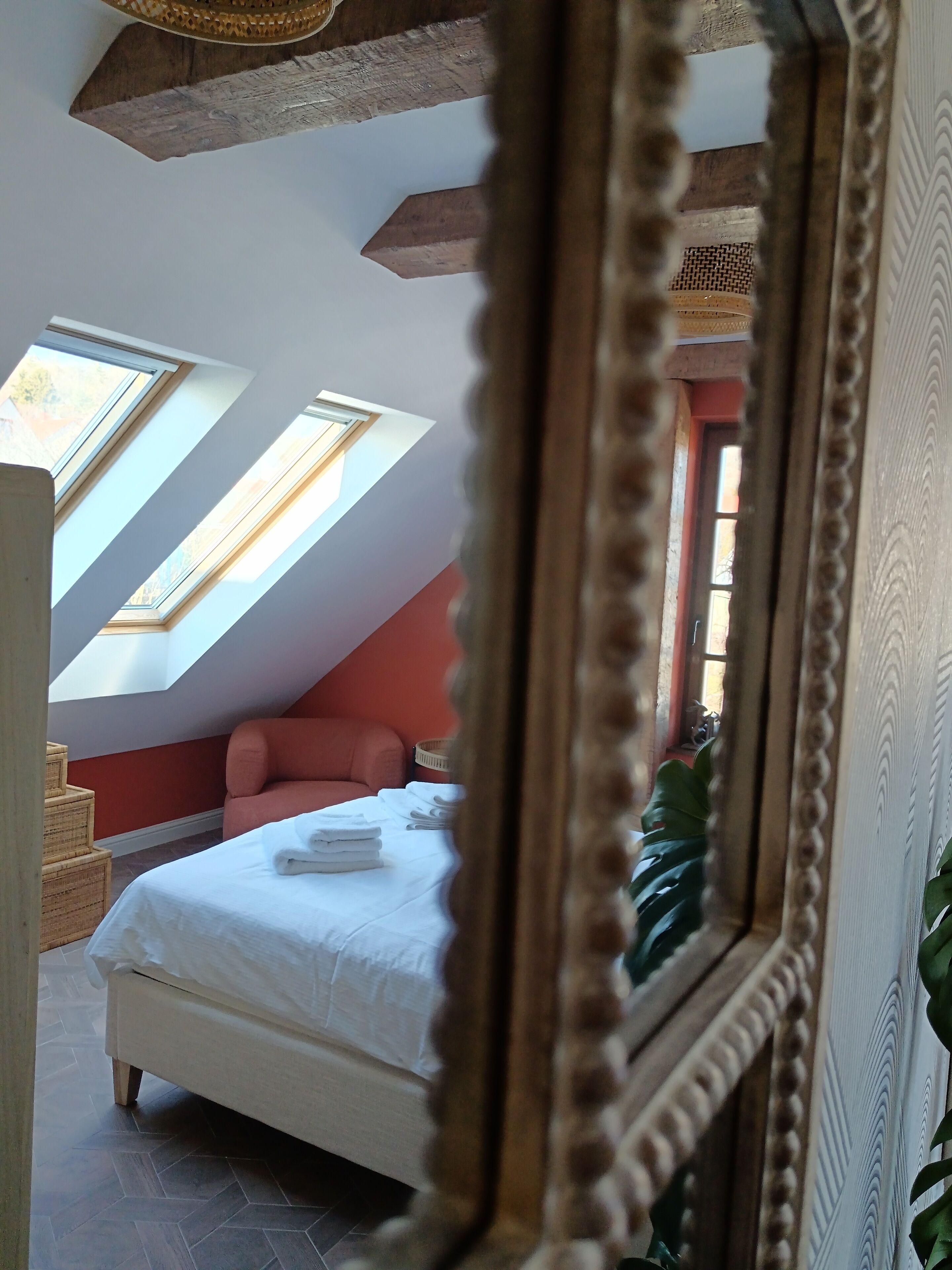 Quarto com cama, parede vermelha e claraboias.