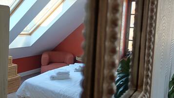 Quarto com cama, parede vermelha e claraboias.