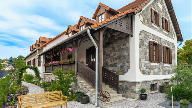 Uma casa de pedra tradicional com escadaria de madeira e um banco no jardim.