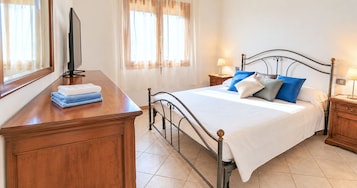 Quarto com cama, mesas de cabeceira, televisão de tela plana e cômoda de madeira.