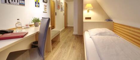 Quarto de hotel com cama, escrivaninha, cadeira, abajur e uma pequena planta.