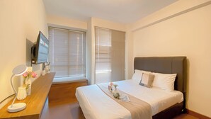 Quarto de hotel com cama, escrivaninha com luminária e televisão na parede.