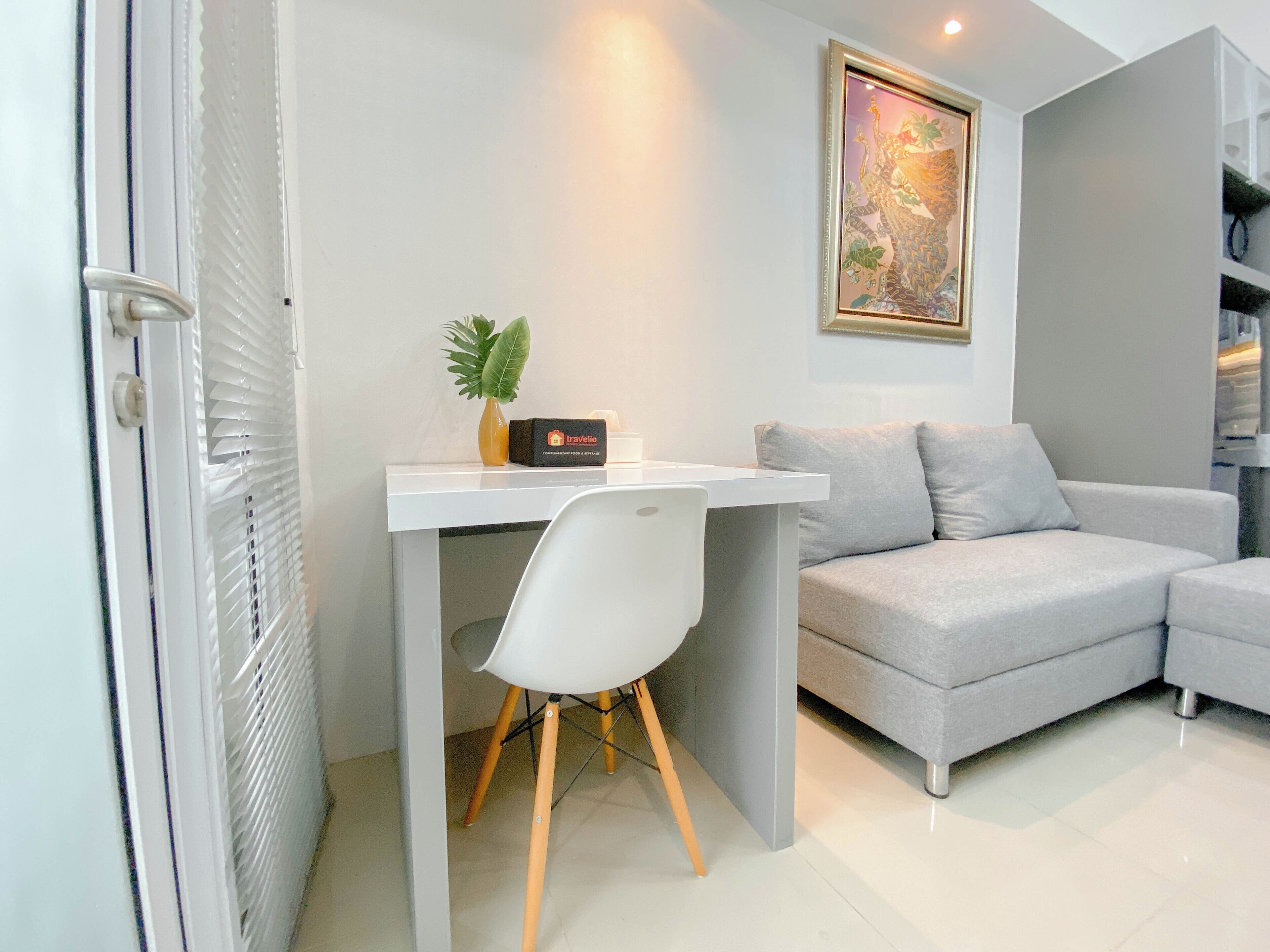 Uma sala de estar moderna com uma escrivaninha branca, um sofá cinza, uma planta pequena e um quadro na parede.