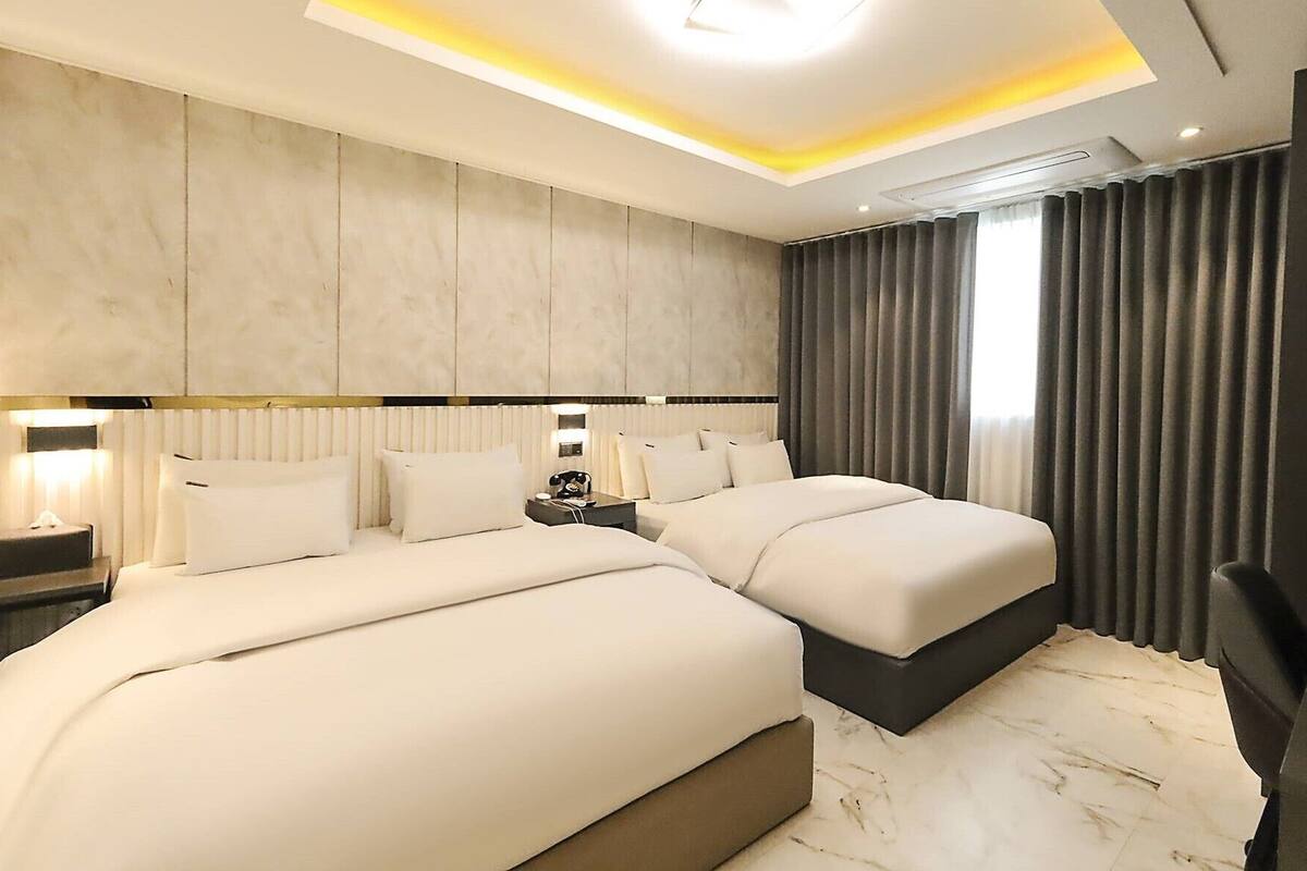 Quarto de hotel moderno com duas camas grandes, piso de mármore e uma janela ampla com cortinas.