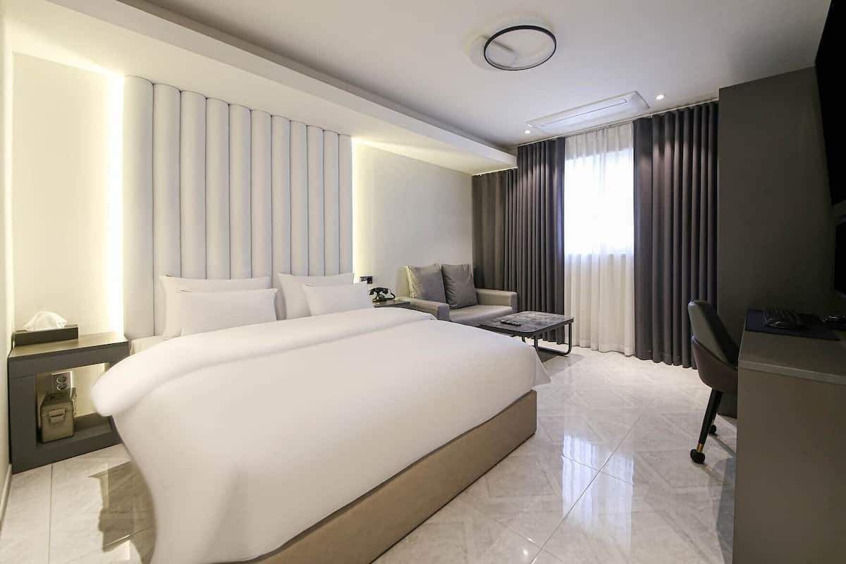 Quarto de hotel moderno com uma cama grande, uma escrivaninha com computador e uma televisão.