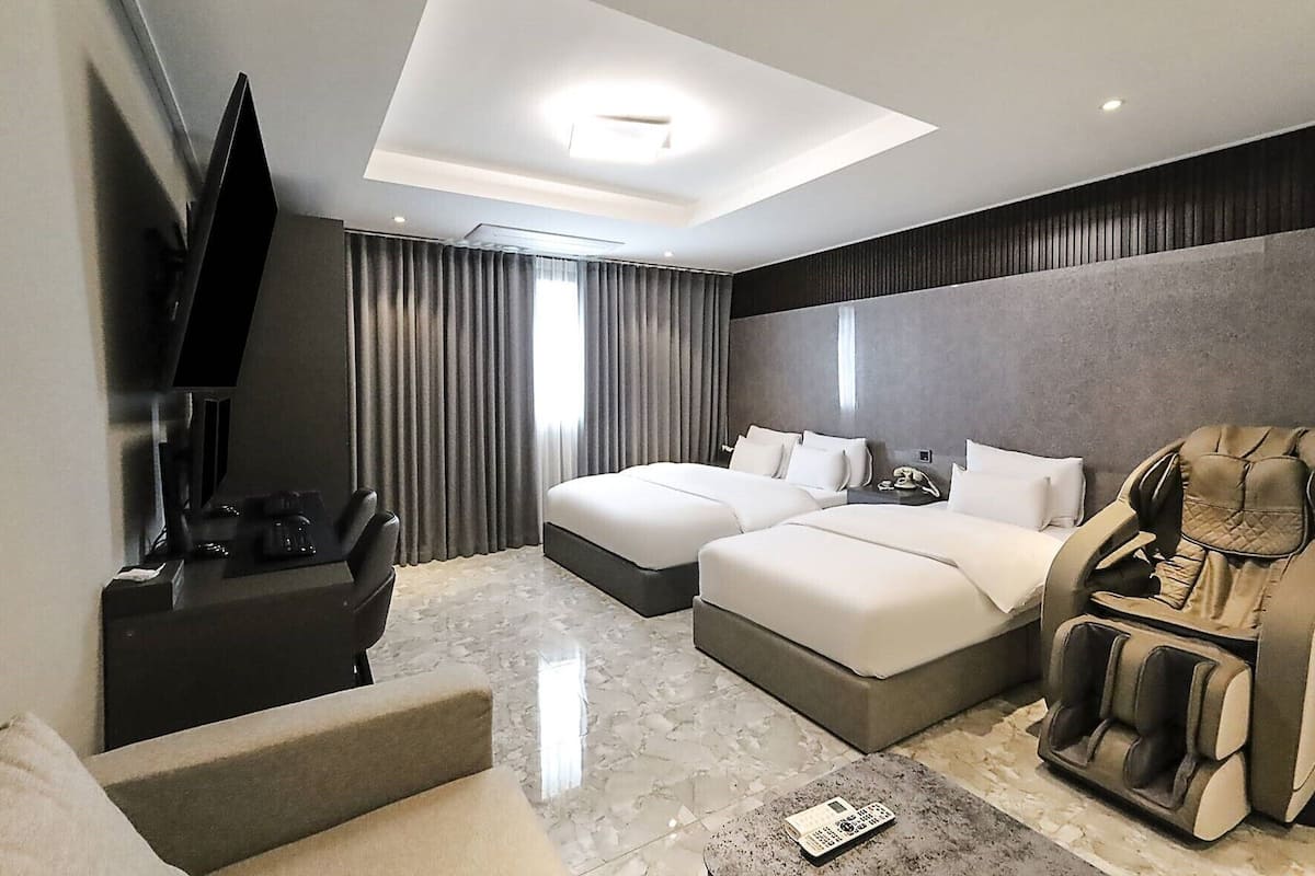 Quarto de hotel moderno com uma cama, uma cadeira de massagem, uma escrivaninha com telefone e uma televisão.