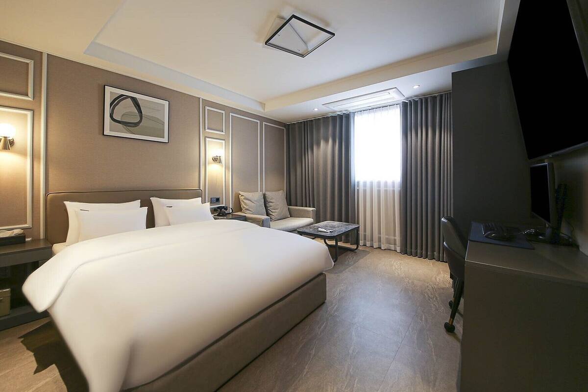 Quarto de hotel com uma cama grande, uma escrivaninha com cadeira, televisão e janela com cortinas.