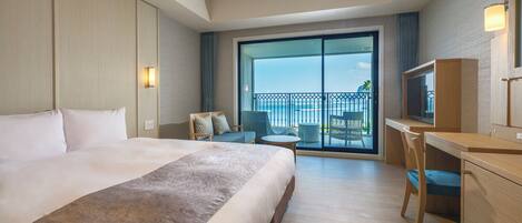 Quarto de hotel com uma cama grande, uma escrivaninha, uma cadeira e uma varanda vista para o mar.