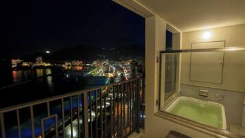 Varanda com vista para a cidade à noite, banheira e um pequeno espaço de estar.