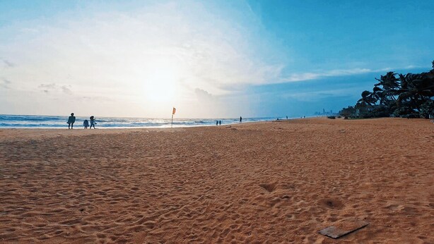 Uma praia com uma bandeira, pessoas caminhando e o oceano ao fundo.