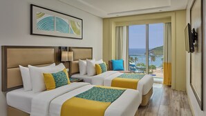 Quarto de hotel com duas camas, uma janela grande com vista para o oceano e uma obra de arte emoldurada na parede.