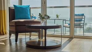 Quarto moderno com sofá de couro marrom, mesa de centro de vidro e vista para o mar através de grandes janelas.