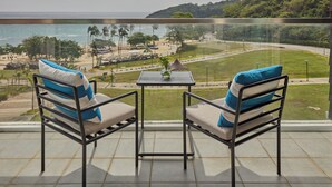 Varanda com duas cadeiras e uma mesa pequena, com vista para a praia e para a estrada.