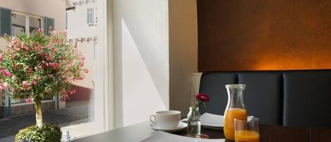 Uma mesa de café da manhã com uma xícara, um copo de suco de laranja e um pequeno vaso com flores.