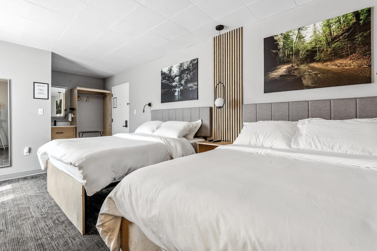 Quarto de hotel com duas camas, um espelho grande, um guarda-roupa e obras de arte nas paredes.