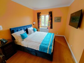 Quarto com cama grande, mesa de cabeceira, janela com cortinas e um quadro na parede.