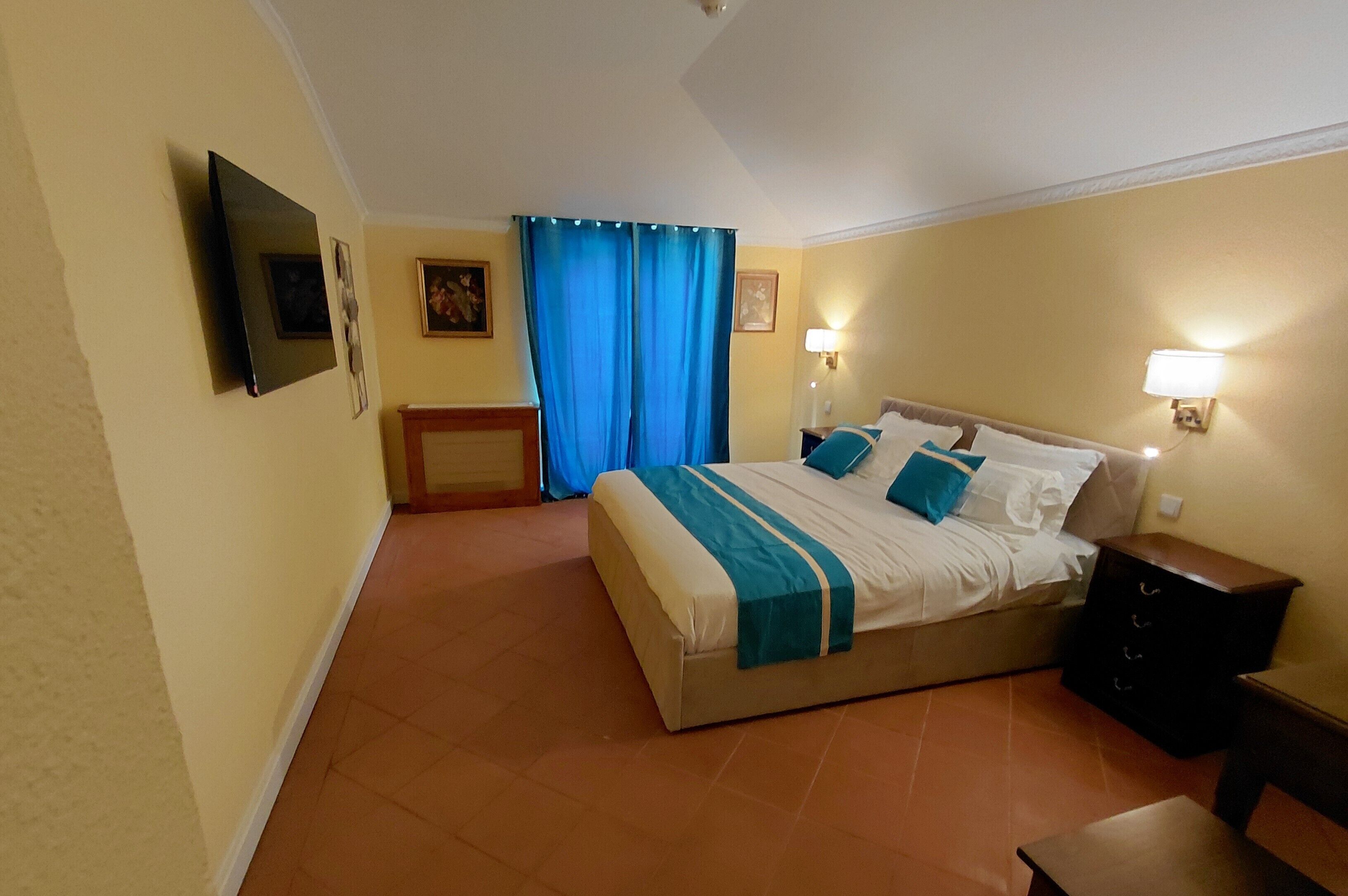 Quarto de hotel com cama, televisão na parede, mesa de cabeceira e abajur.