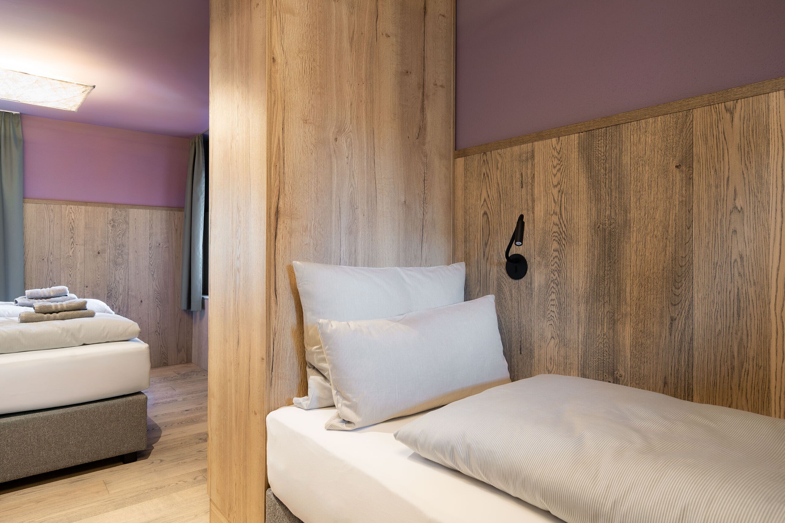 Quarto com cabeceira de madeira, cama com roupa de cama branca e mesa de cabeceira com abajur.