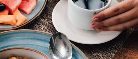 Uma mesa de café da manhã com xícara de café, pratos de frutas e tigela de cereal.